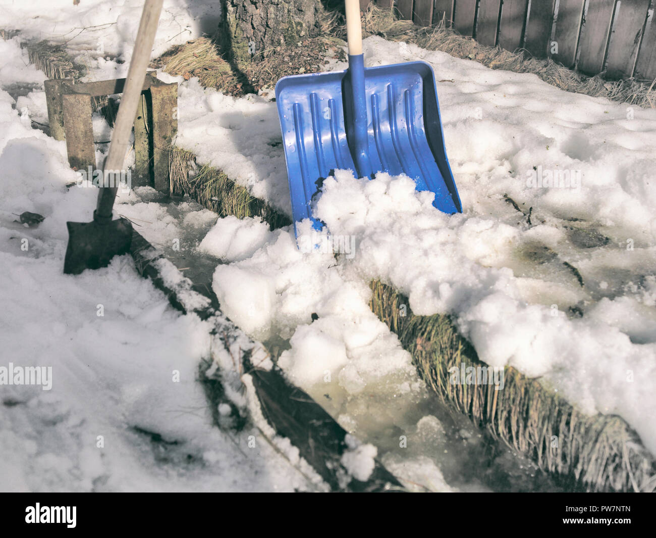 Two shovels and trench full of malting snow, filtered image Stock Photo ...
