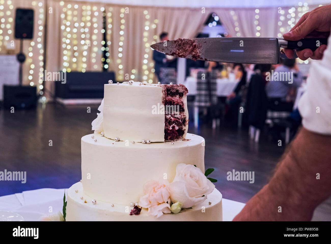 Groom cuts the multitiered white mastic wedding cake in a banquet hall ...
