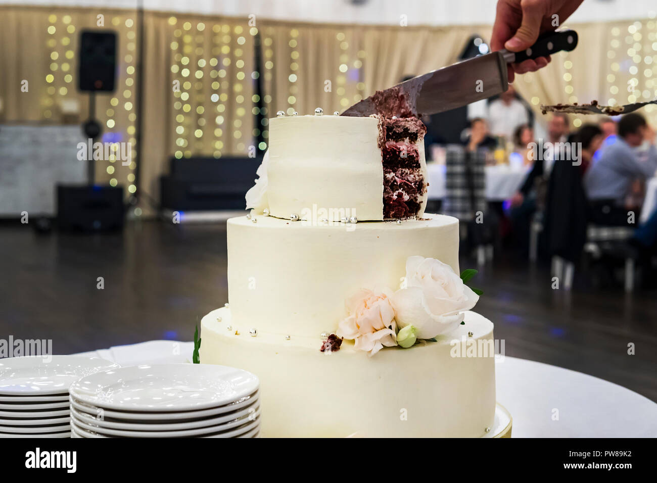 Cutting the first tier of white mastic wedding cake in banquet hall ...