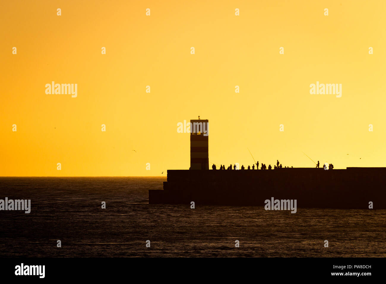 A group of people stand near a lighthouse before sunset Stock Photo - Alamy