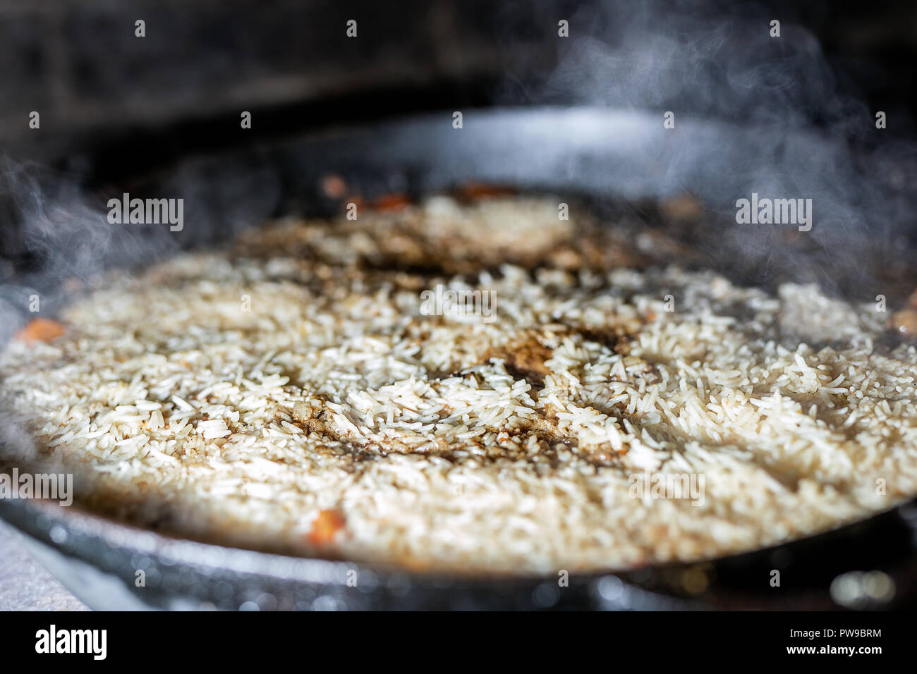 cooking Rice for pilaw or paella in iron cauldron over open fire. Smoke ...