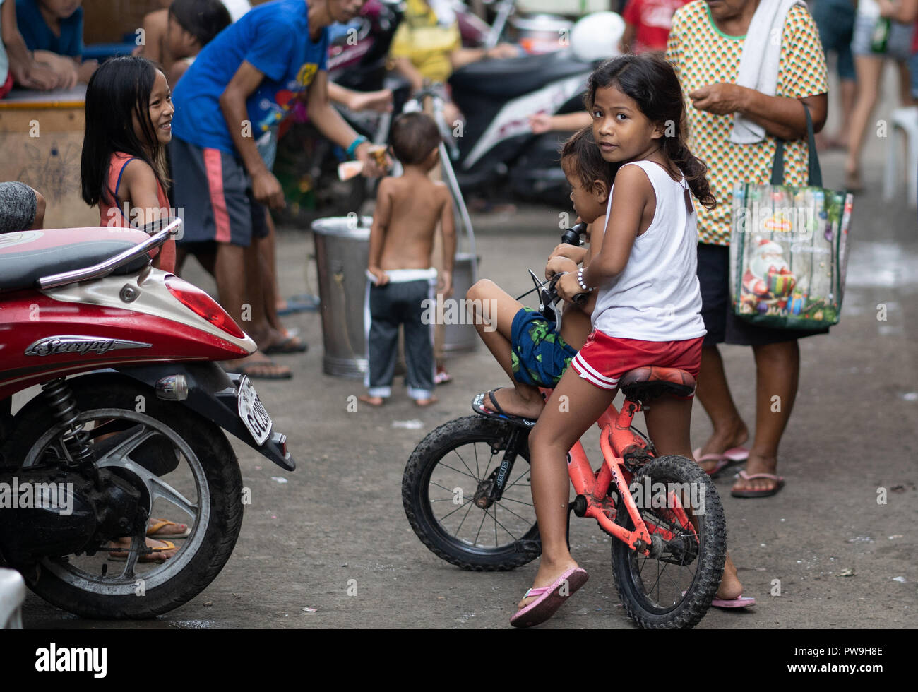 A young Filipino girl riding a bicycle with another child within a slum ...
