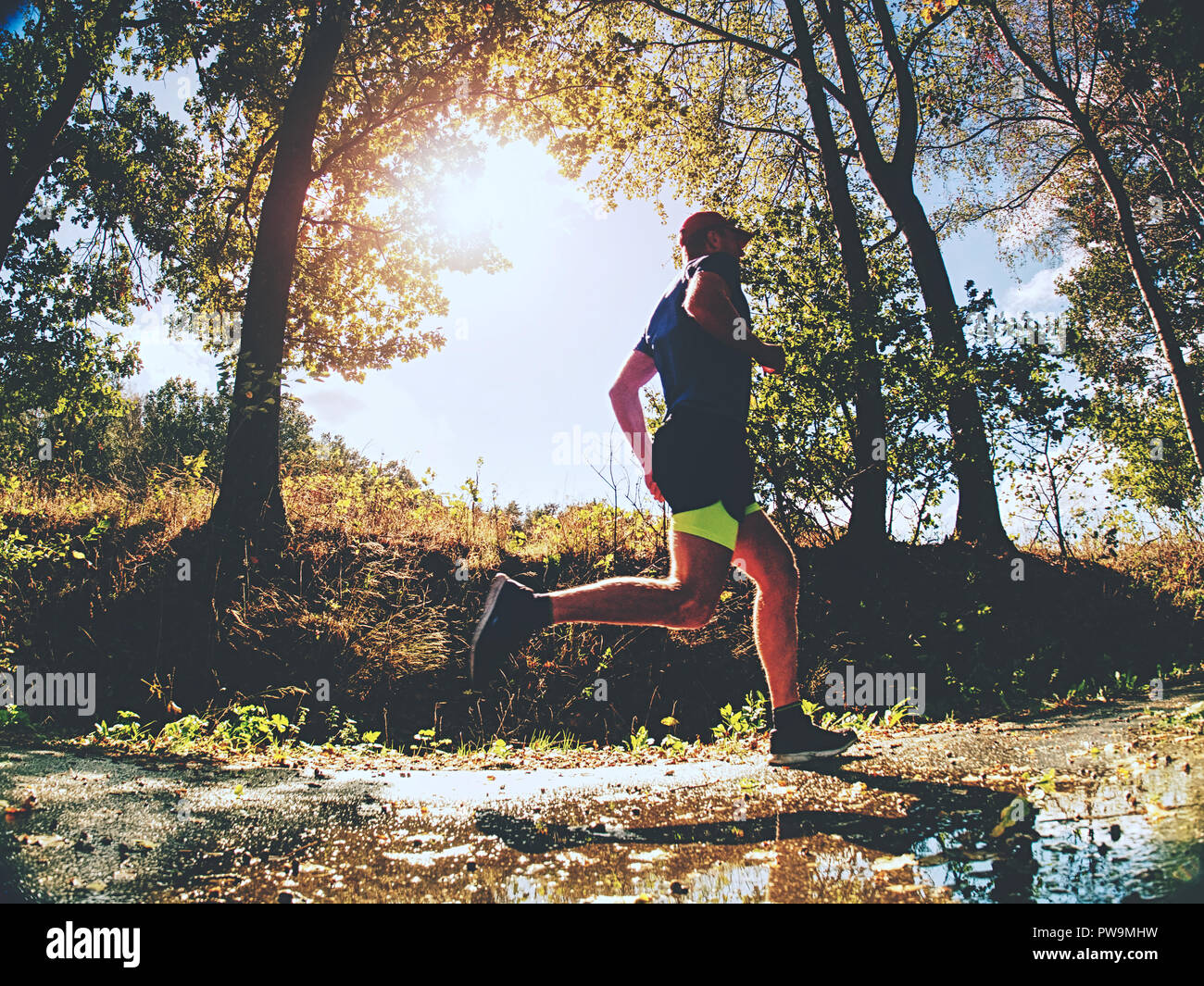 Jogging tall sports man in trees shadows with sun light behind him ...