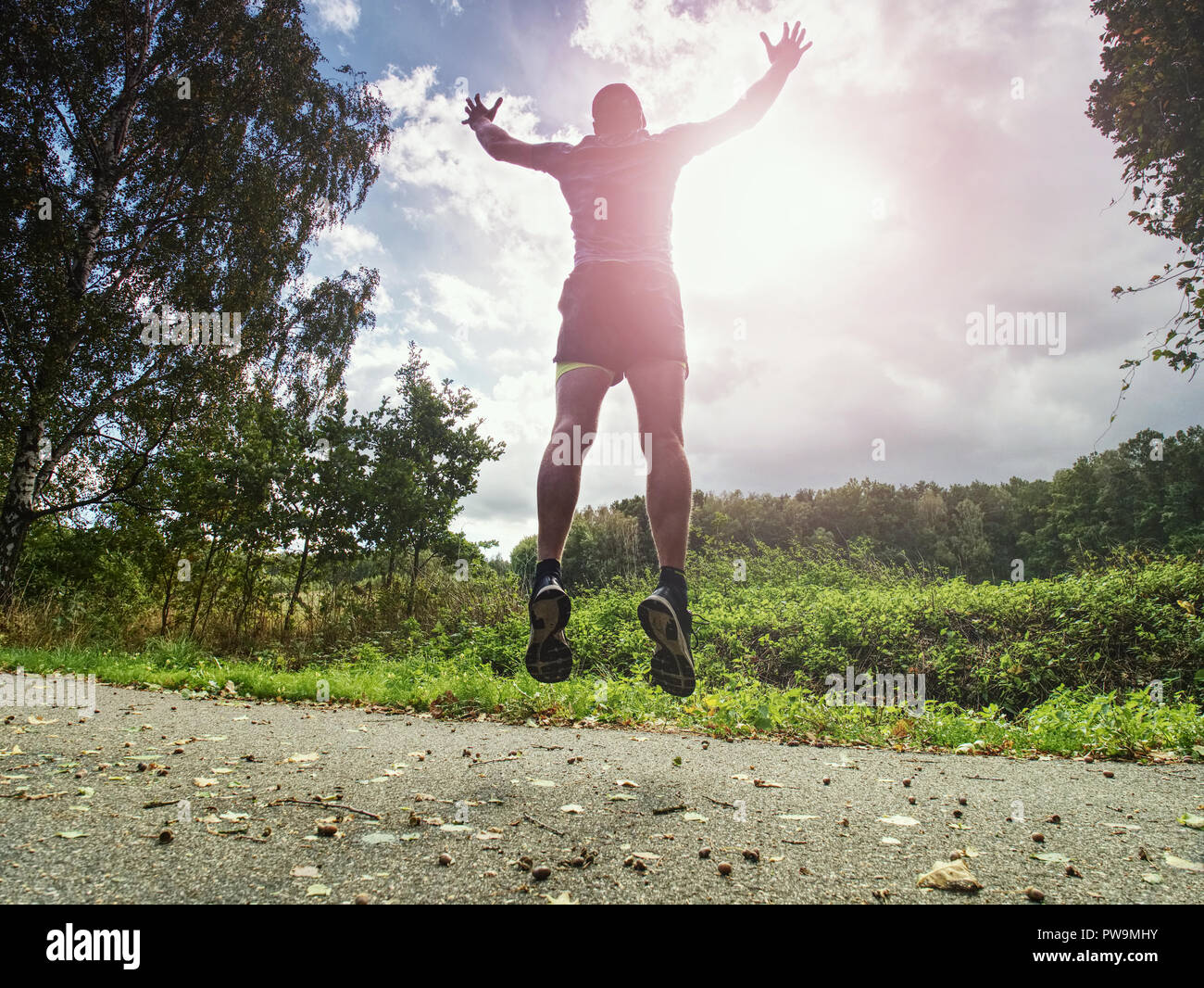 Jogging tall sports man in trees shadows with sun light behind him ...
