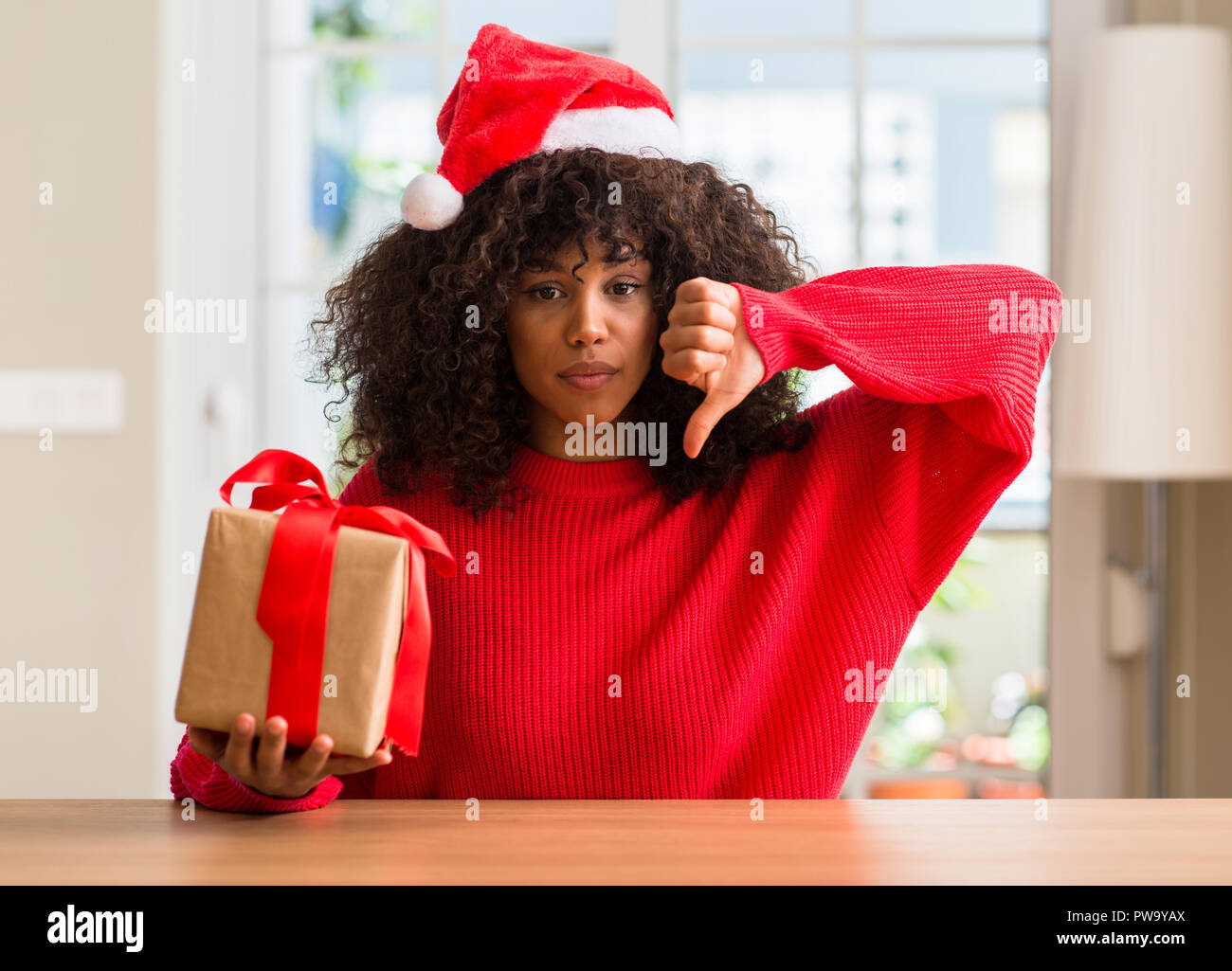African american woman holding present wearing christmas red hat with ...