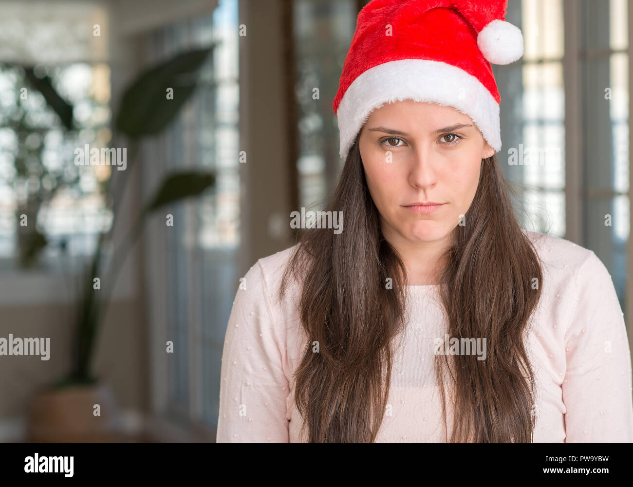 Beautiful young woman wearing Santa Claus hat at home skeptic and nervous, frowning upset ...