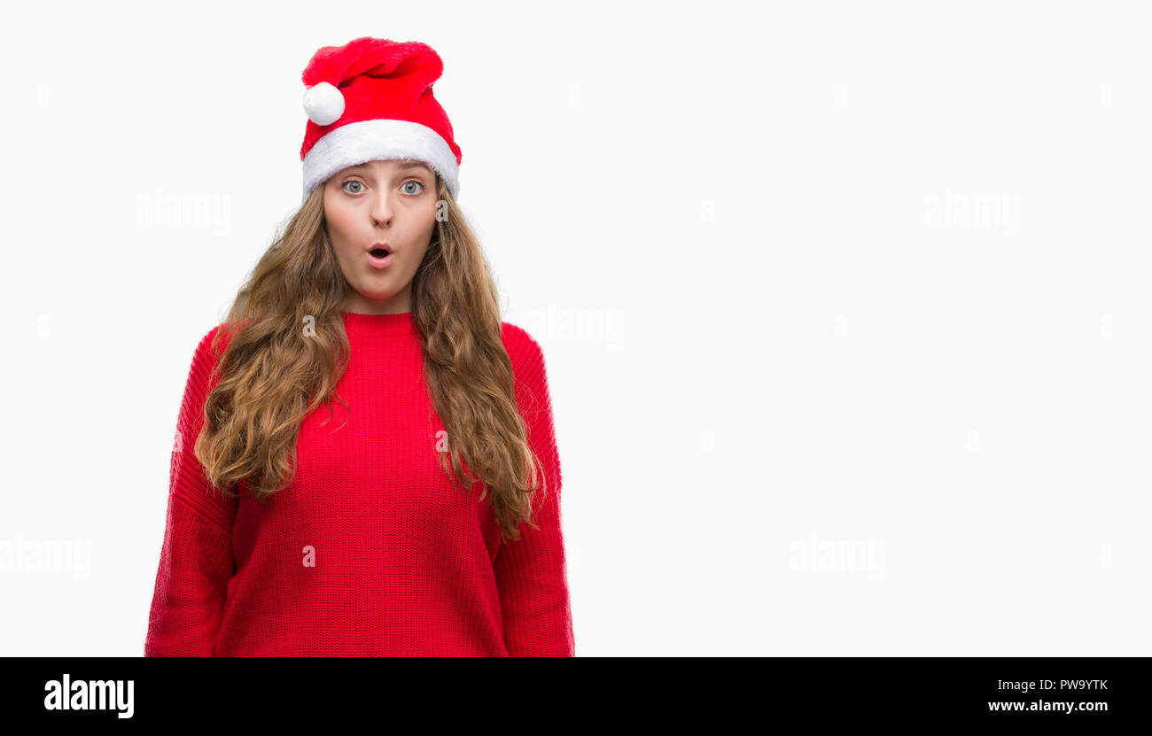 Young blonde woman wearing santa claus hat scared in shock with a ...
