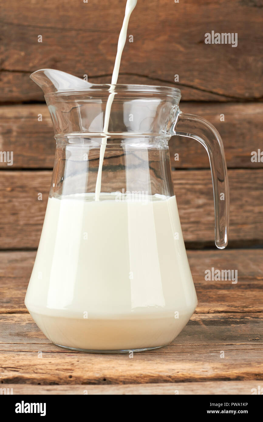 Milk pouring into a jug. Filling a glass pitcher with fresh milk. Eco ...