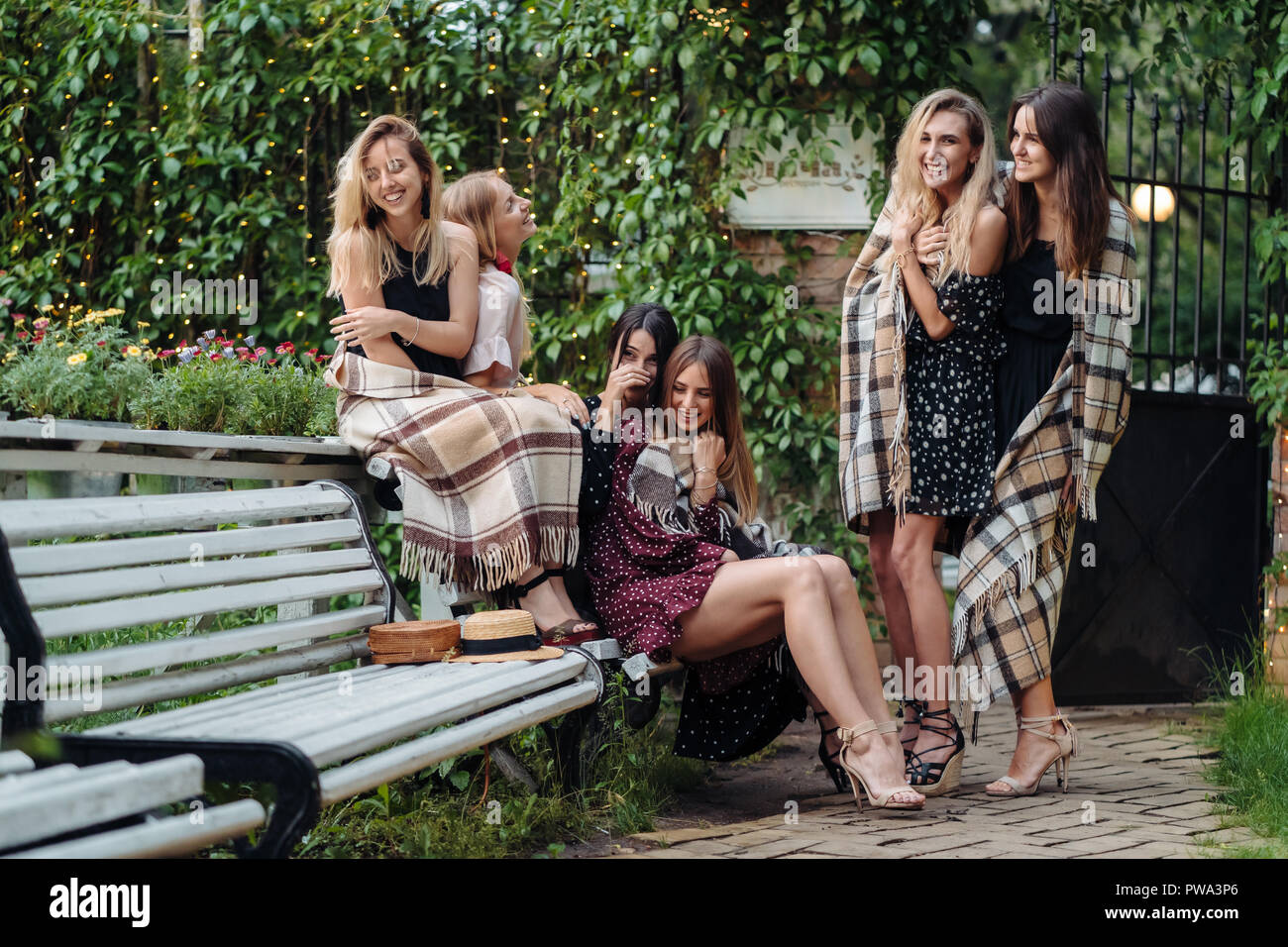 Six beautiful girls wrapped in plaid posing on camera in park on bench ...