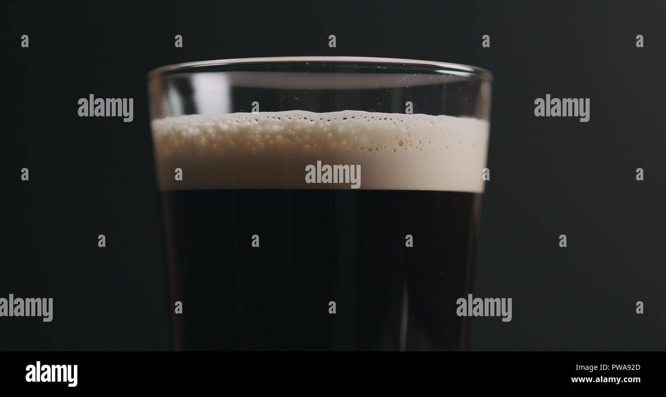 Closeup dark stout beer with bubbles over black background, wide photo ...