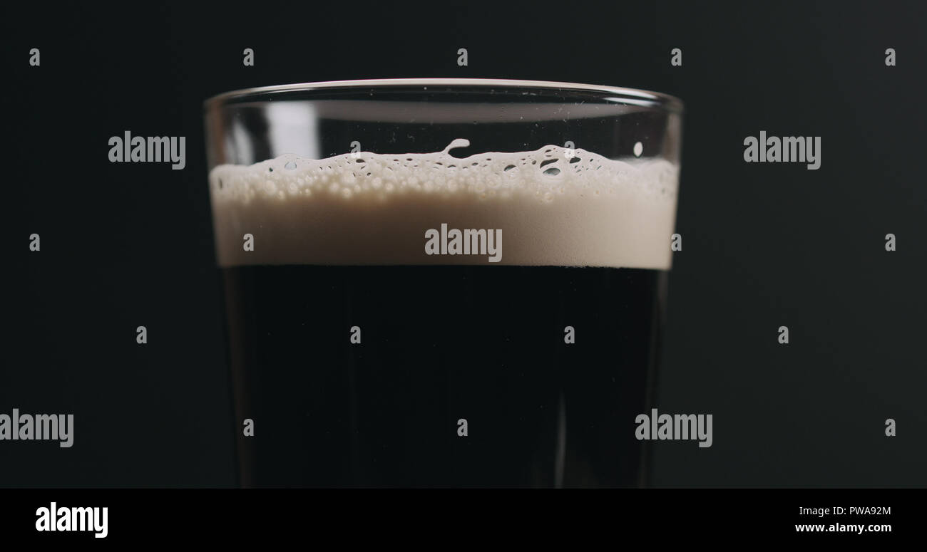 Closeup dark stout beer with bubbles over black background, wide photo ...