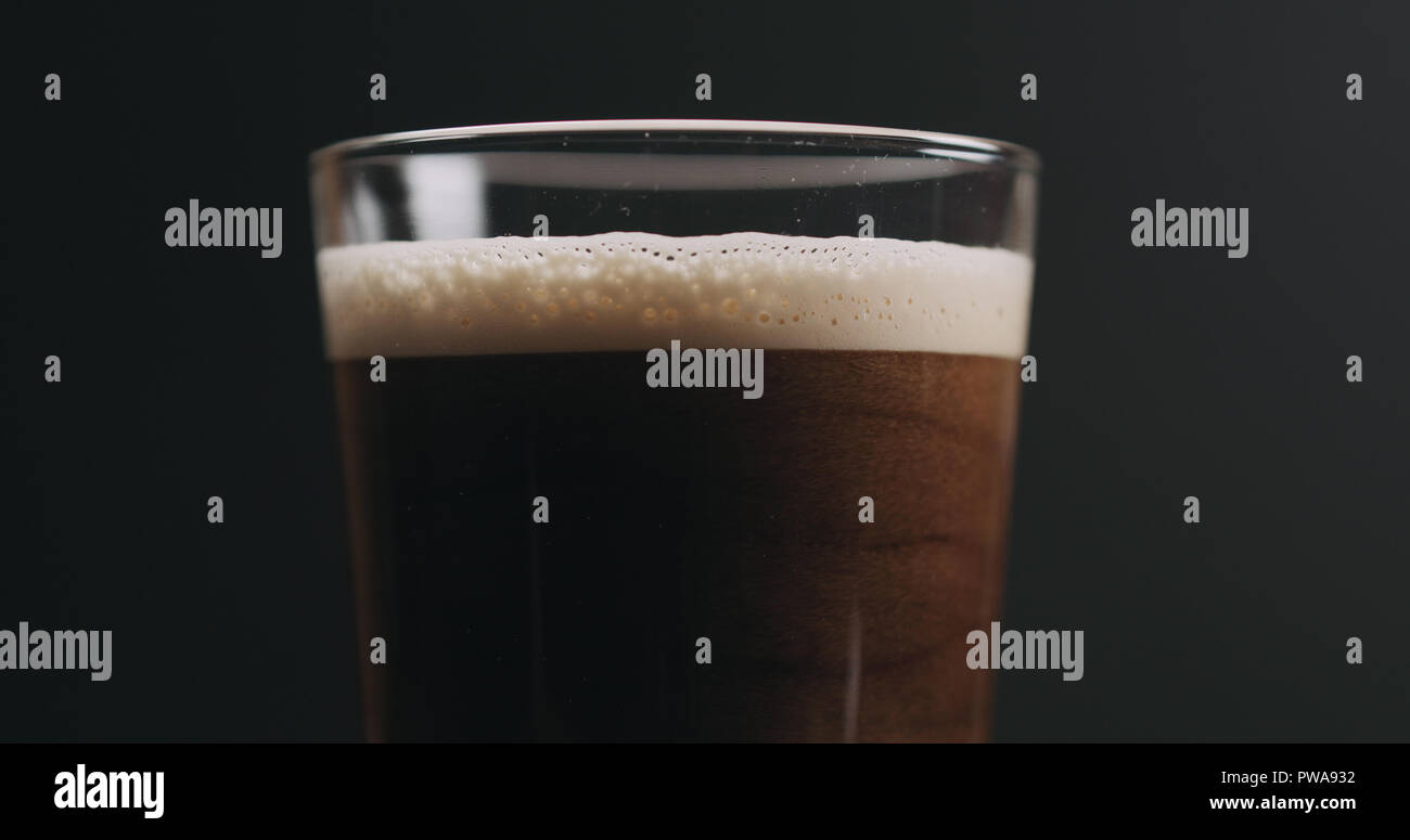 Closeup dark stout beer with bubbles over black background, wide photo ...