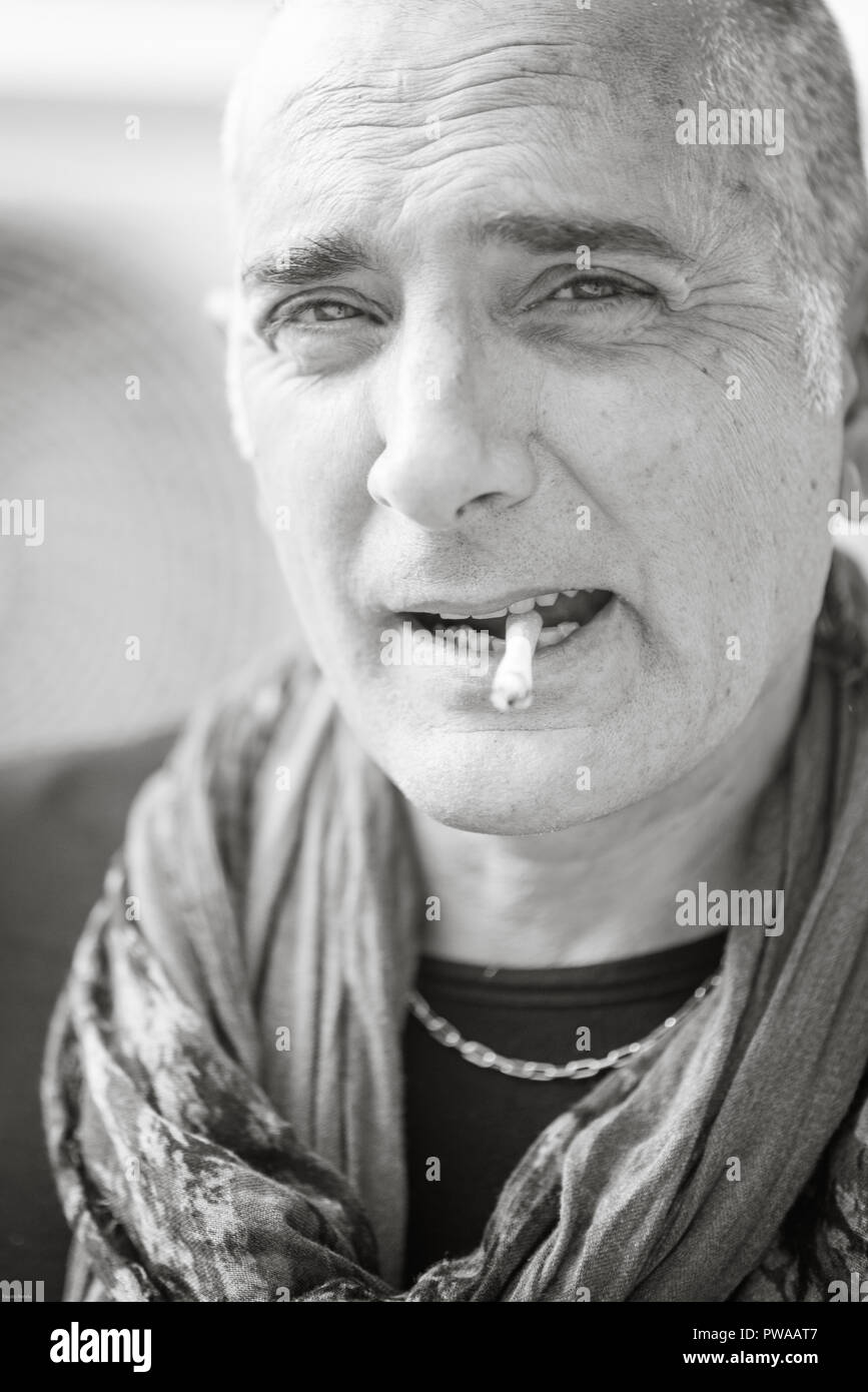 A 50y man is smoking a cigarette. Black and white. The fan coil of an ...