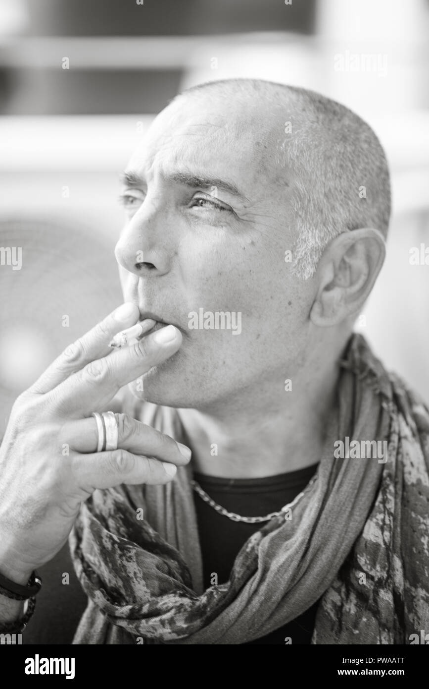 A 50y man is smoking a cigarette. Black and white. The fan coil of an ...