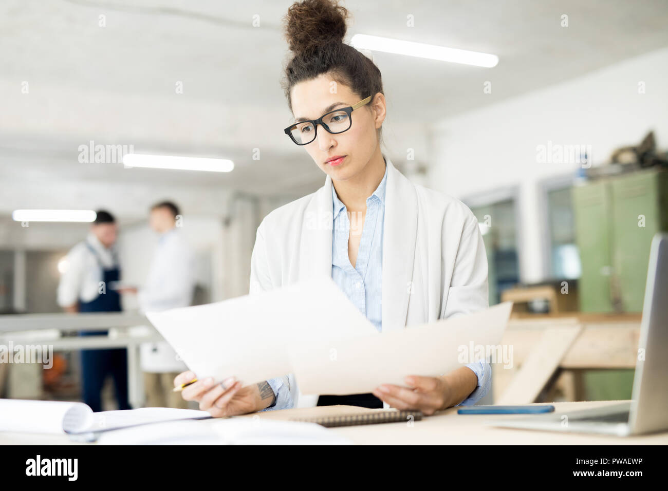 Young female expert in whitecoat reading working papers while sitting ...