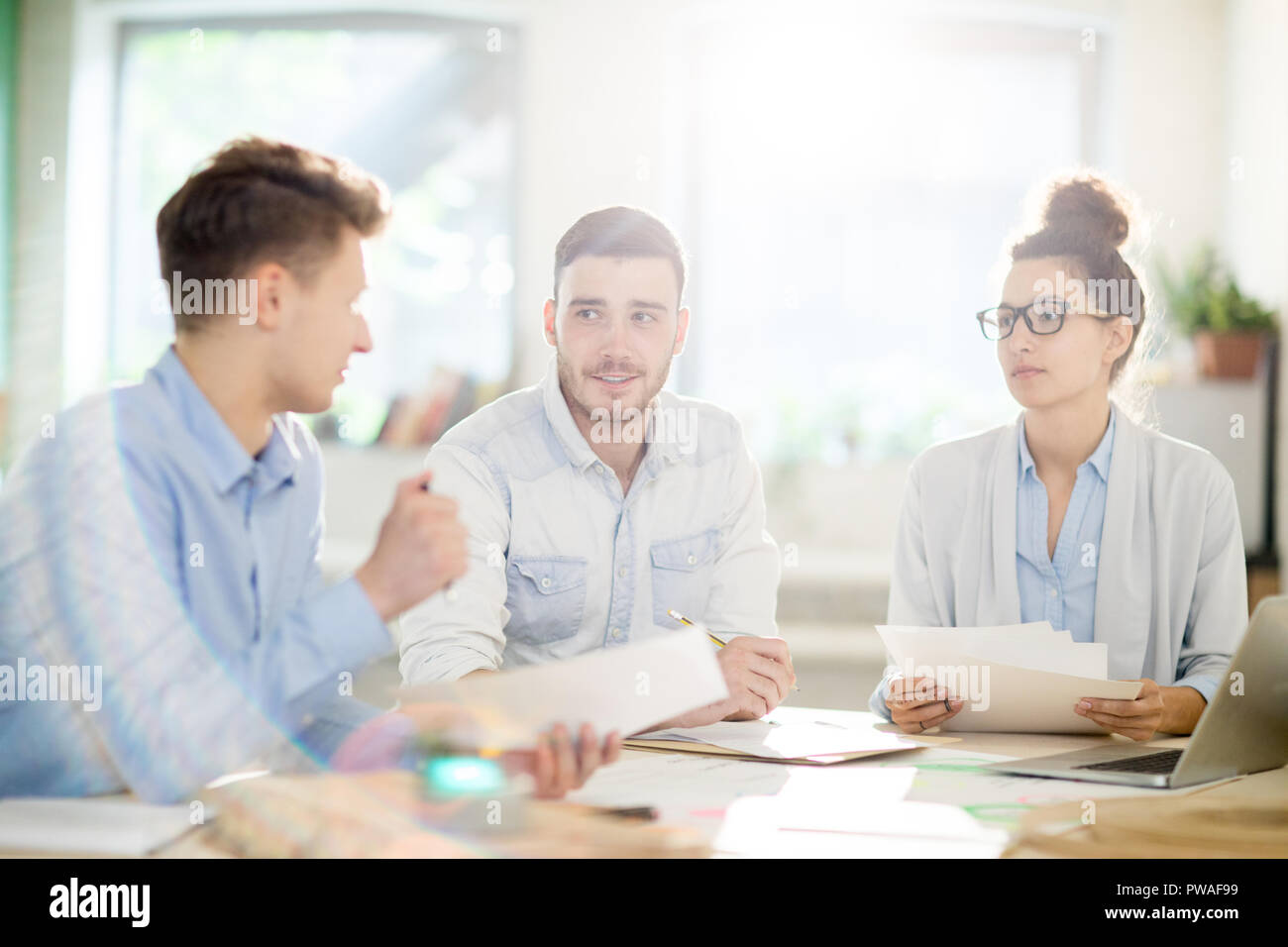 Meeting of three young professionals with papers sitting by table and ...