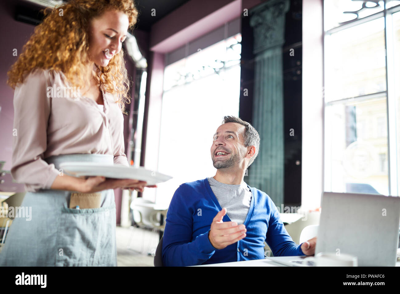 Happy networking businessman looking at waitress bringing him his order ...