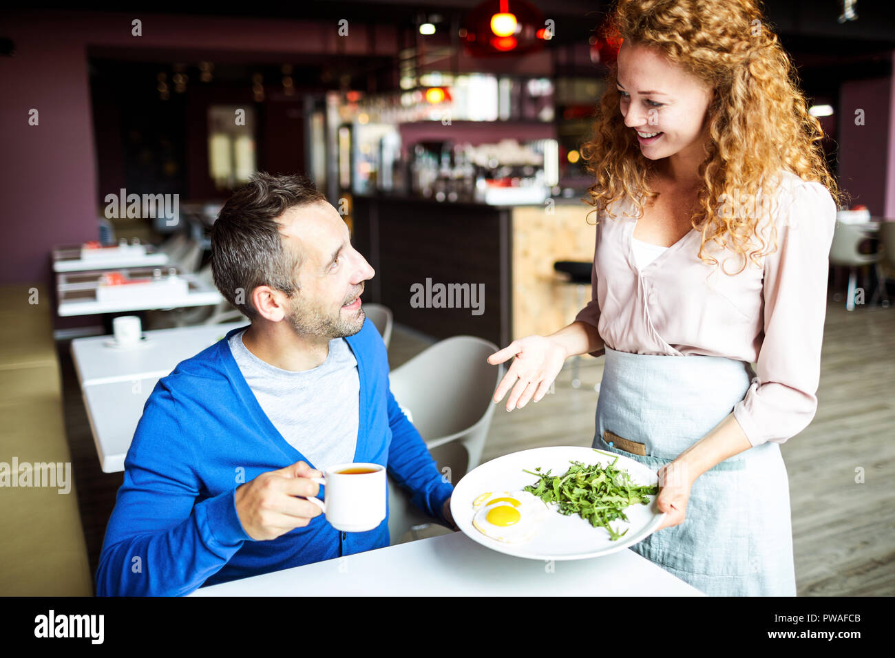 Young waitress bringing businessman his breakfast consisting of fried ...