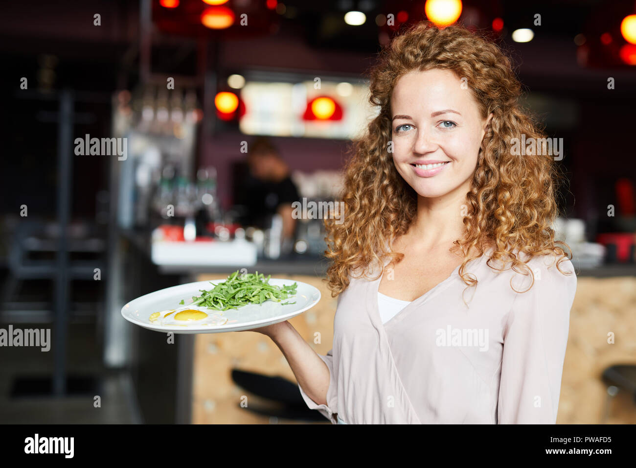Happy waitress in casualwear carrying plate with order of client while ...