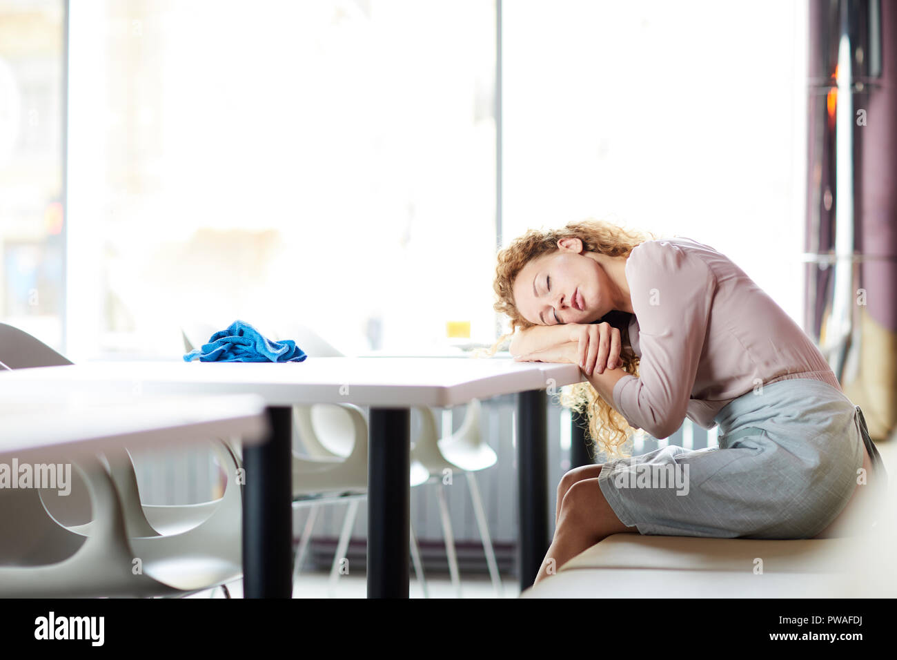 Tired young waitress sleeping on table in the middle of hard working ...