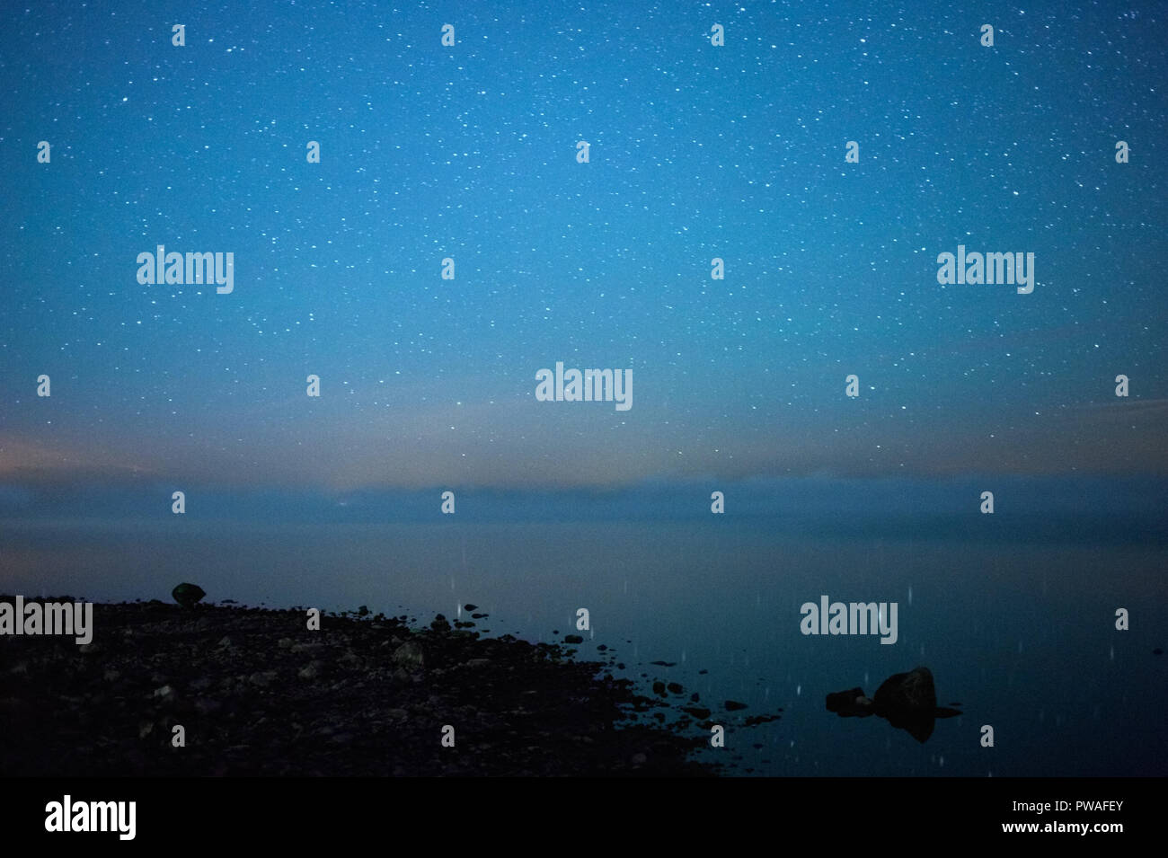 Starry night at rocky lake shore. Fog over water in horizon Stock Photo ...