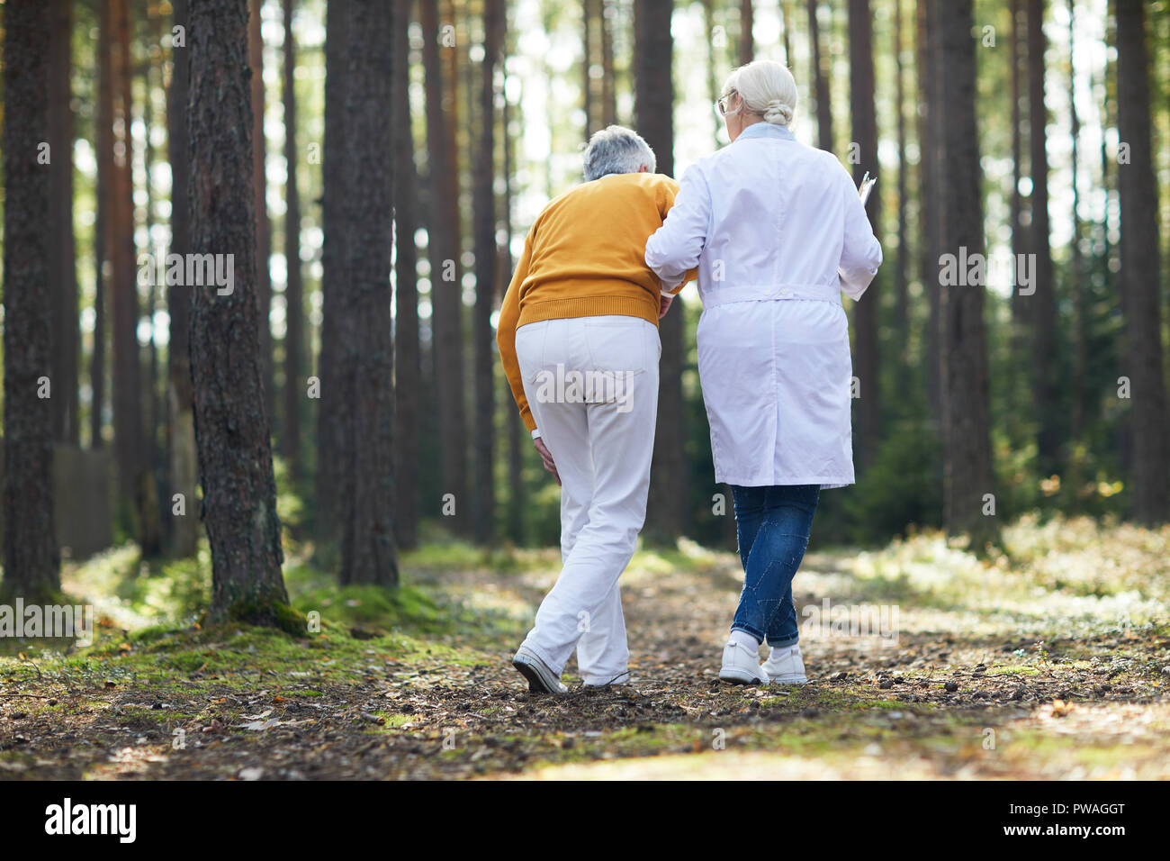 Female clinician in whitecoat helping sick man to walk while both ...