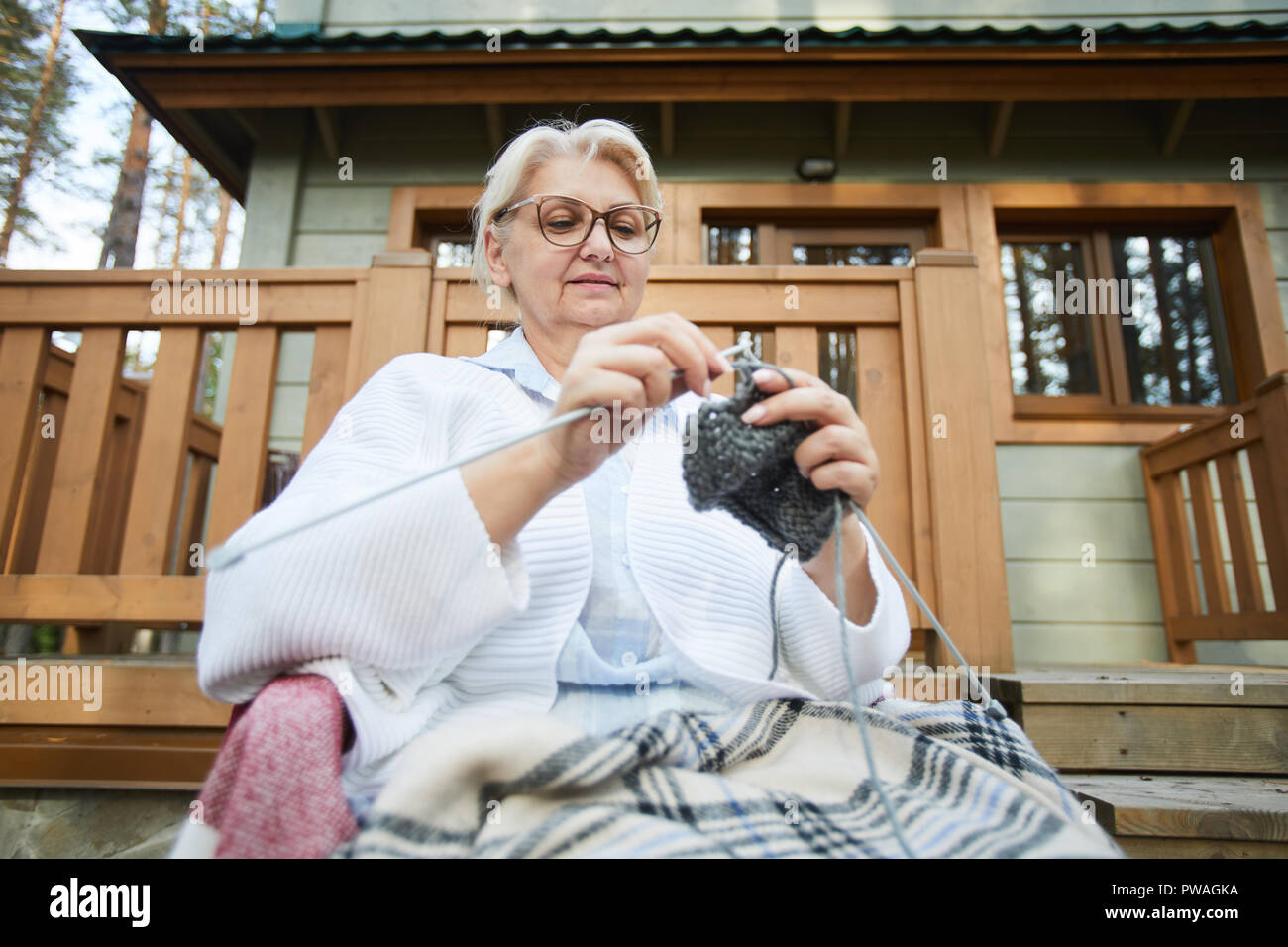 Mature woman relaxing in rocking chair by terrace of cottage on summer ...