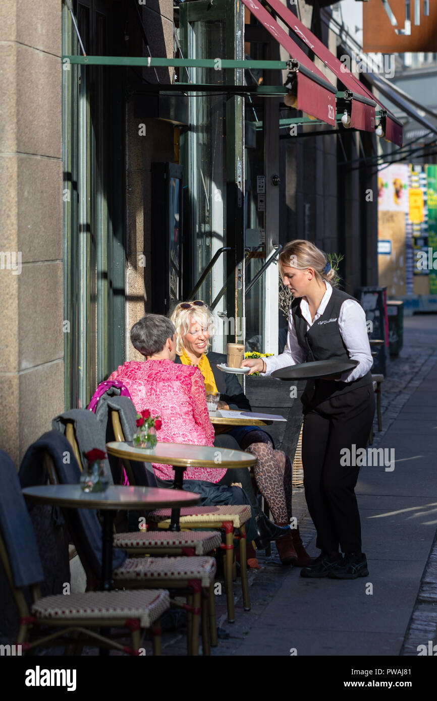 Waitress serving coffee for two women sitting outside a cafe in a small ...