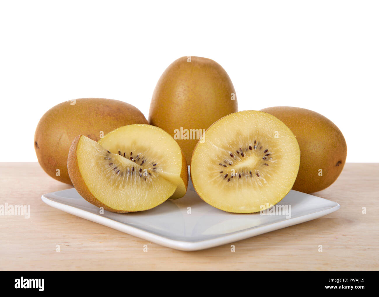 Sungold kiwi sliced in half with whole fruit behind on white plate on ...