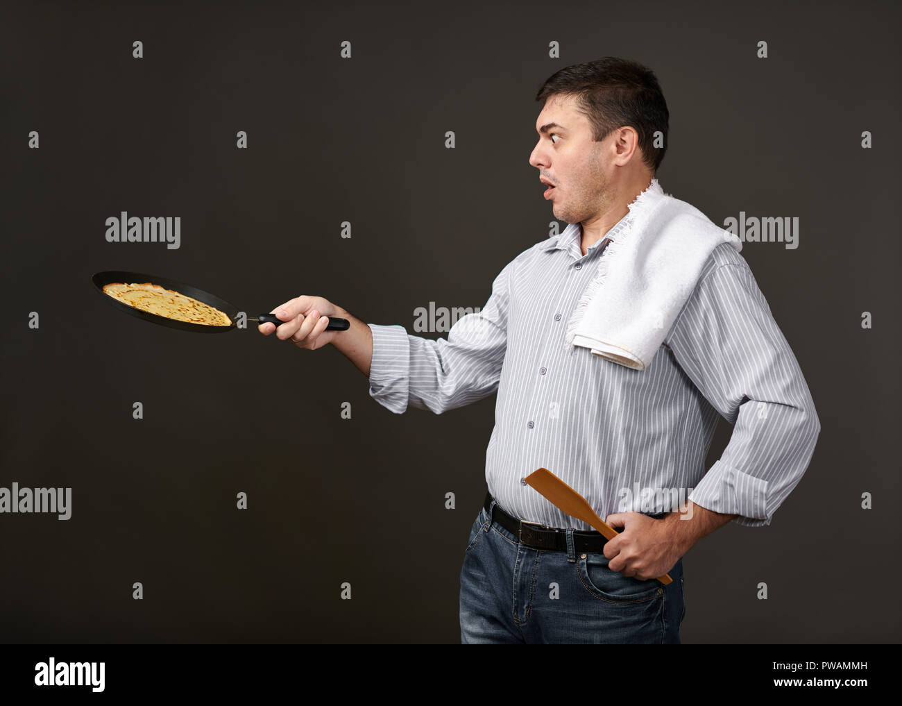 man posing with a pancake in a pan, white shirt and pants, gray ...