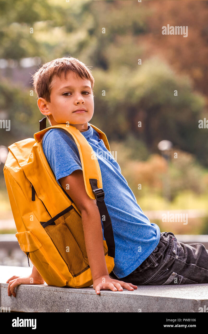 Kid with backpack sitting outdoors and looking to camera Stock Photo ...