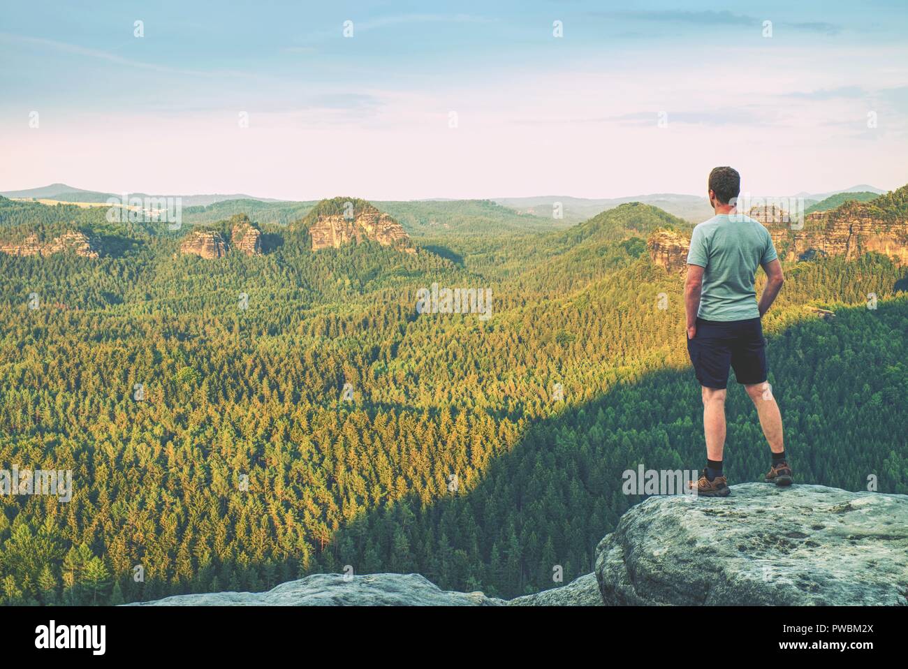 Tall man in outdoor clothes stands alone on the peak of rock. Hiker ...