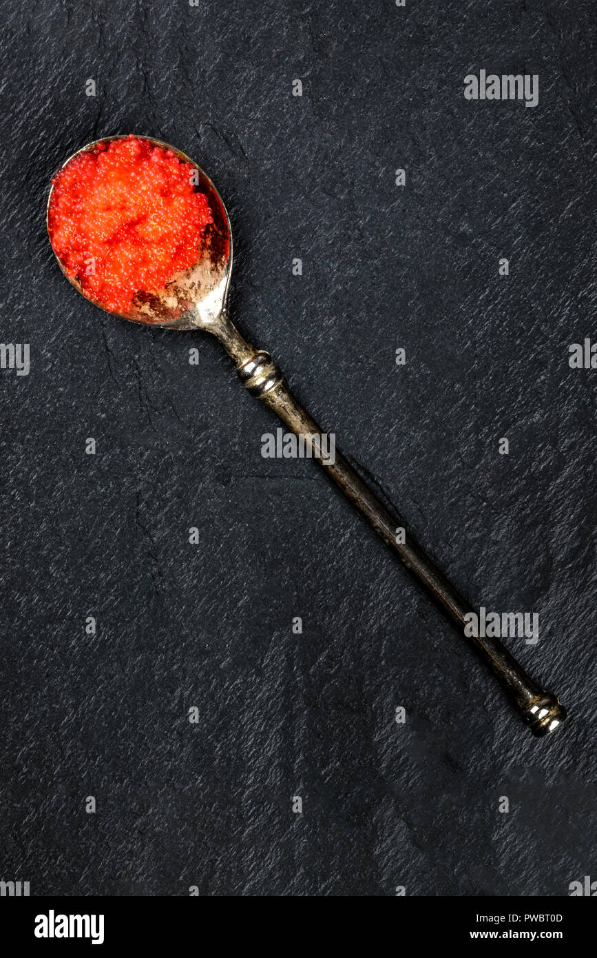 Red fish caviar in a vintage spoon, shot from the top on a black ...