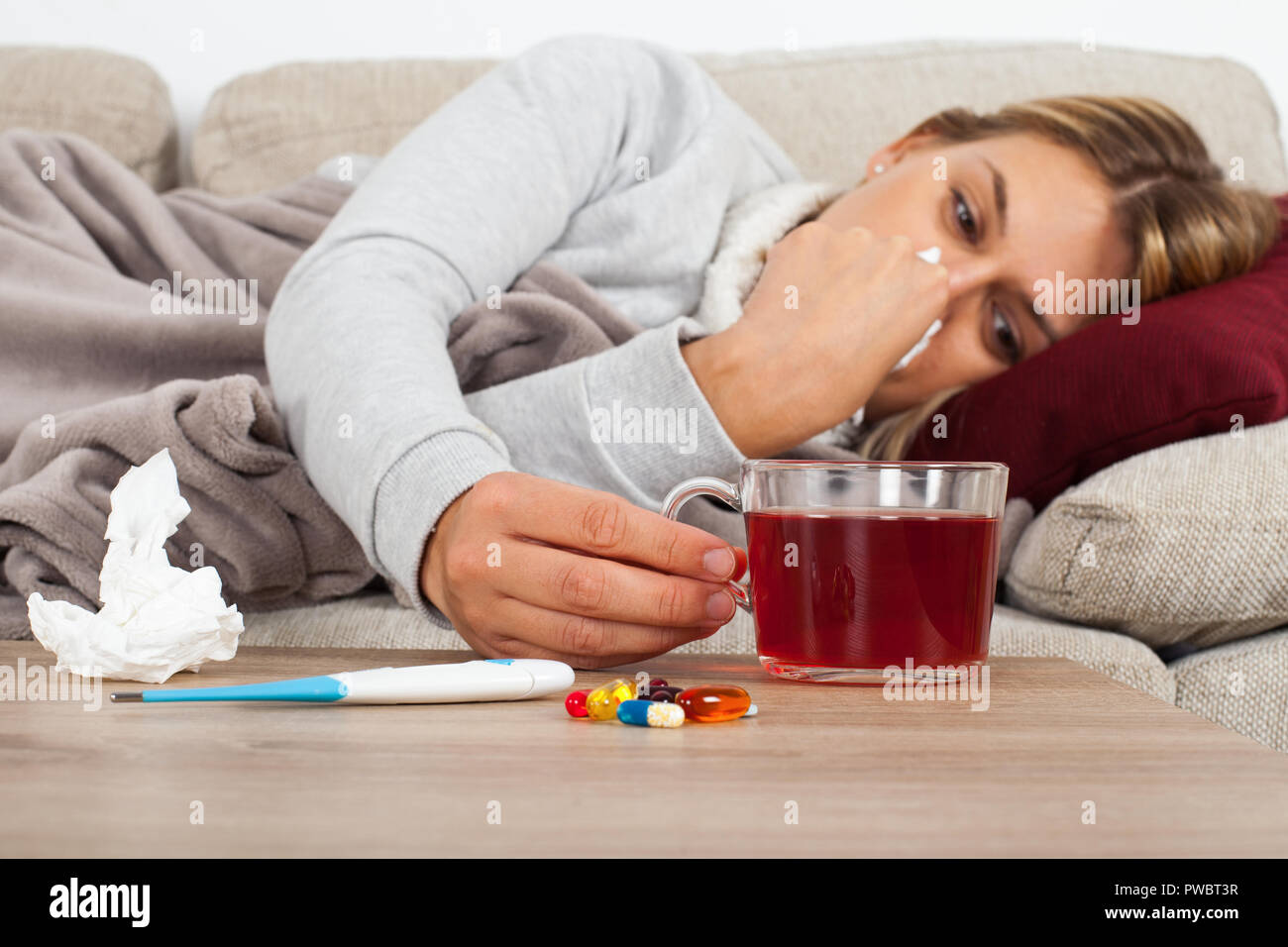 Sick woman lying on the couch wrapped in a warm blanket - medication ...