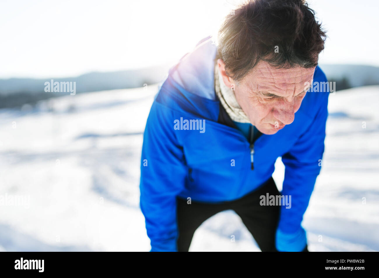 A portrait of senior man standing after the run in winter nature, hands ...