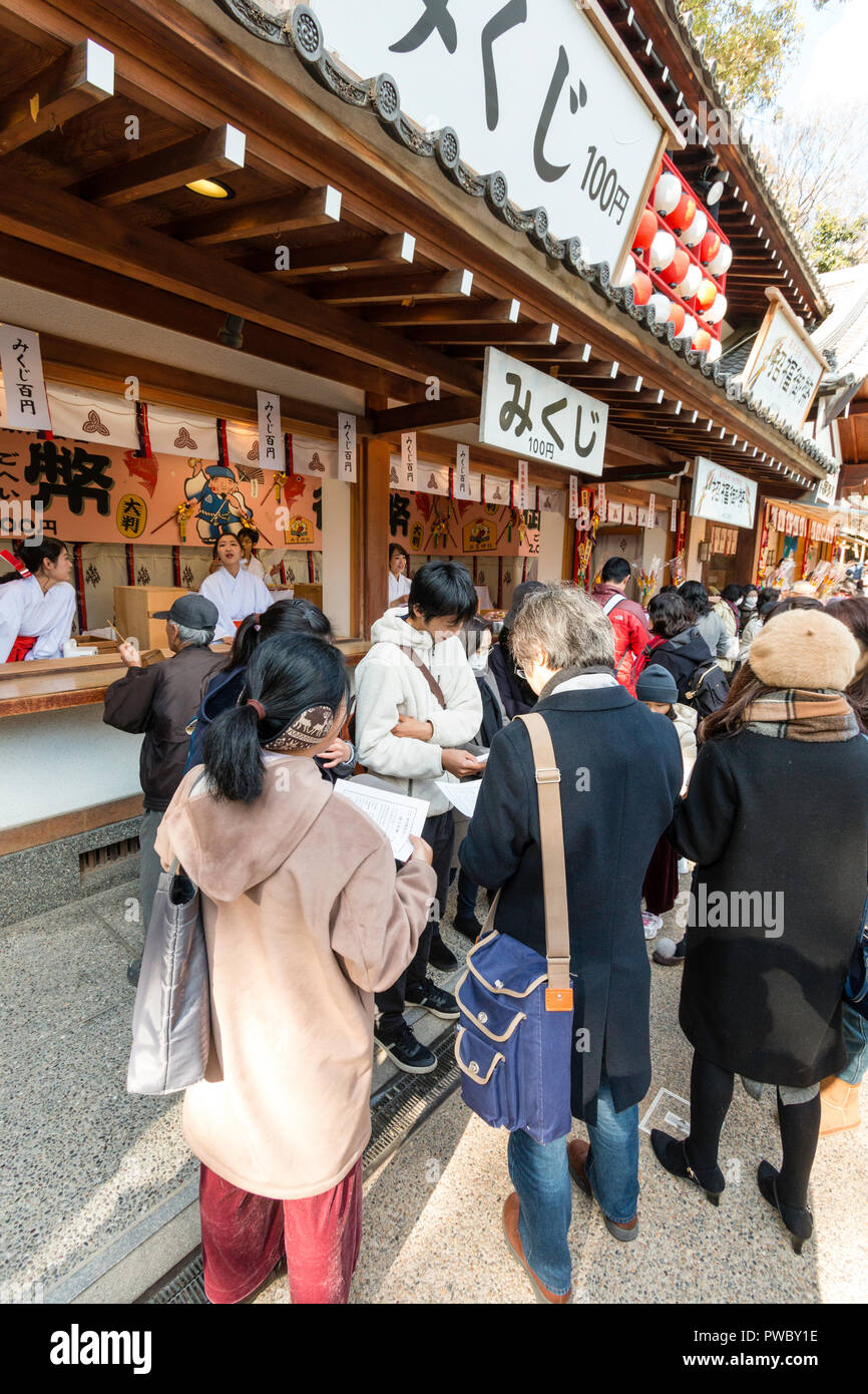 Japanese new year, shogatsu. People standing by shrine counter reading Omikuji fortune paper ...