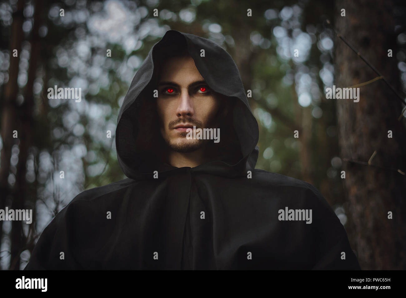 the vampire in the hood with glowing eyes in the forest Stock Photo - Alamy