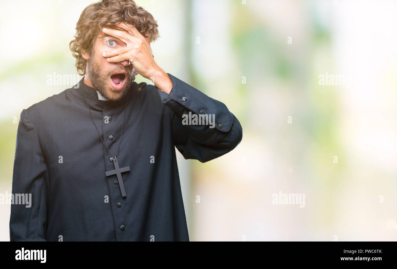 Handsome hispanic catholic priest man over isolated background peeking ...