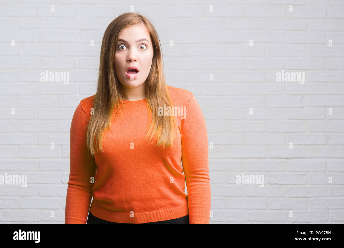 Young adult woman over white brick wall scared in shock with a surprise ...