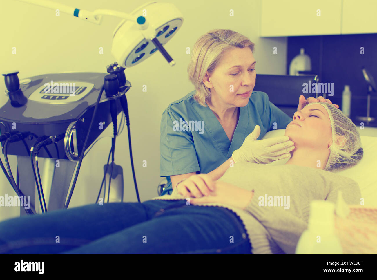 Professional cosmetician examining face skin of girl in clinic of ...
