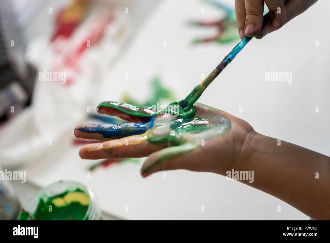 Child painting its hands with colorful paint using a paintbrush in a ...
