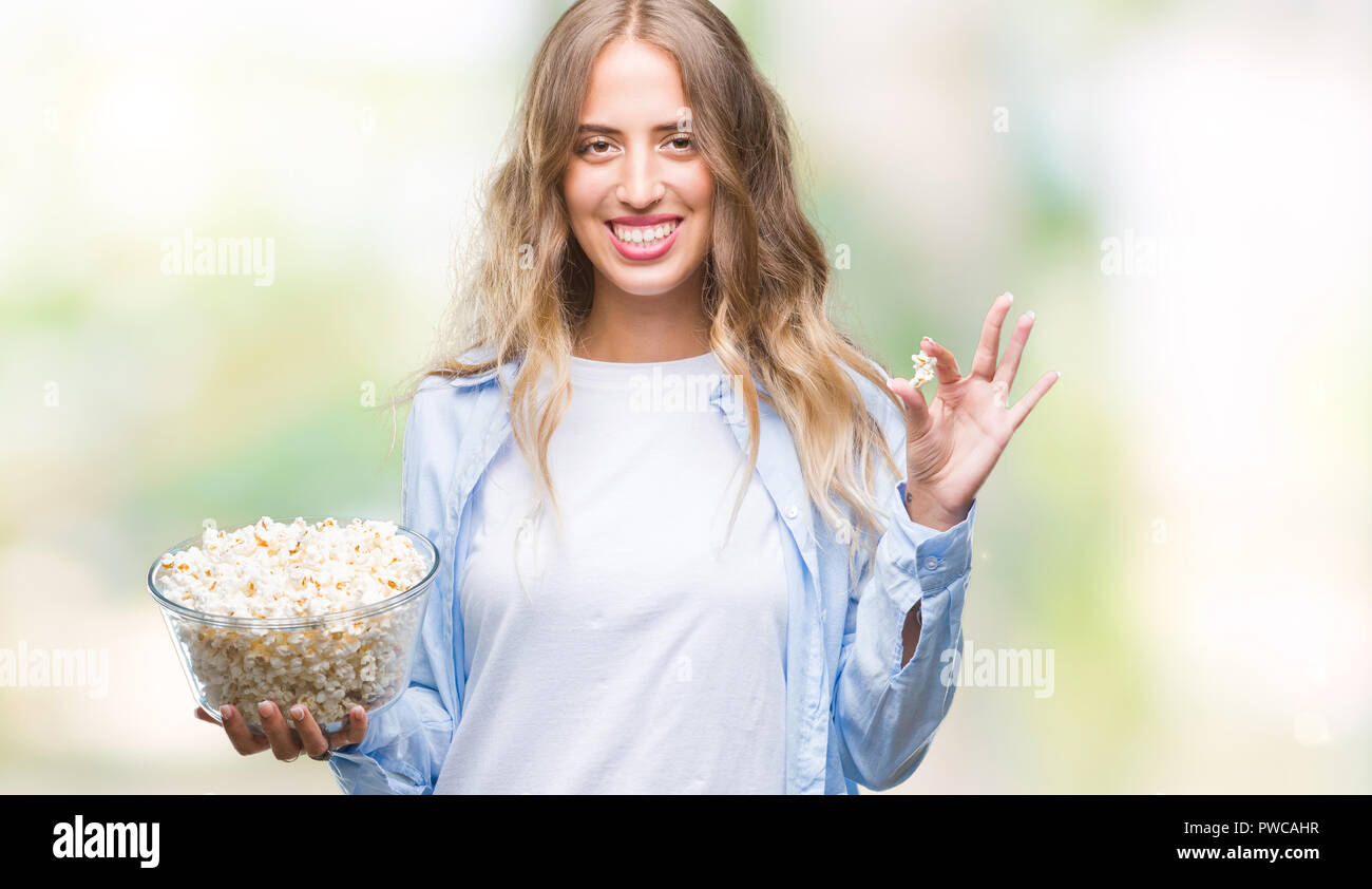 Beautiful young blonde woman eating popcorn over isolated background ...