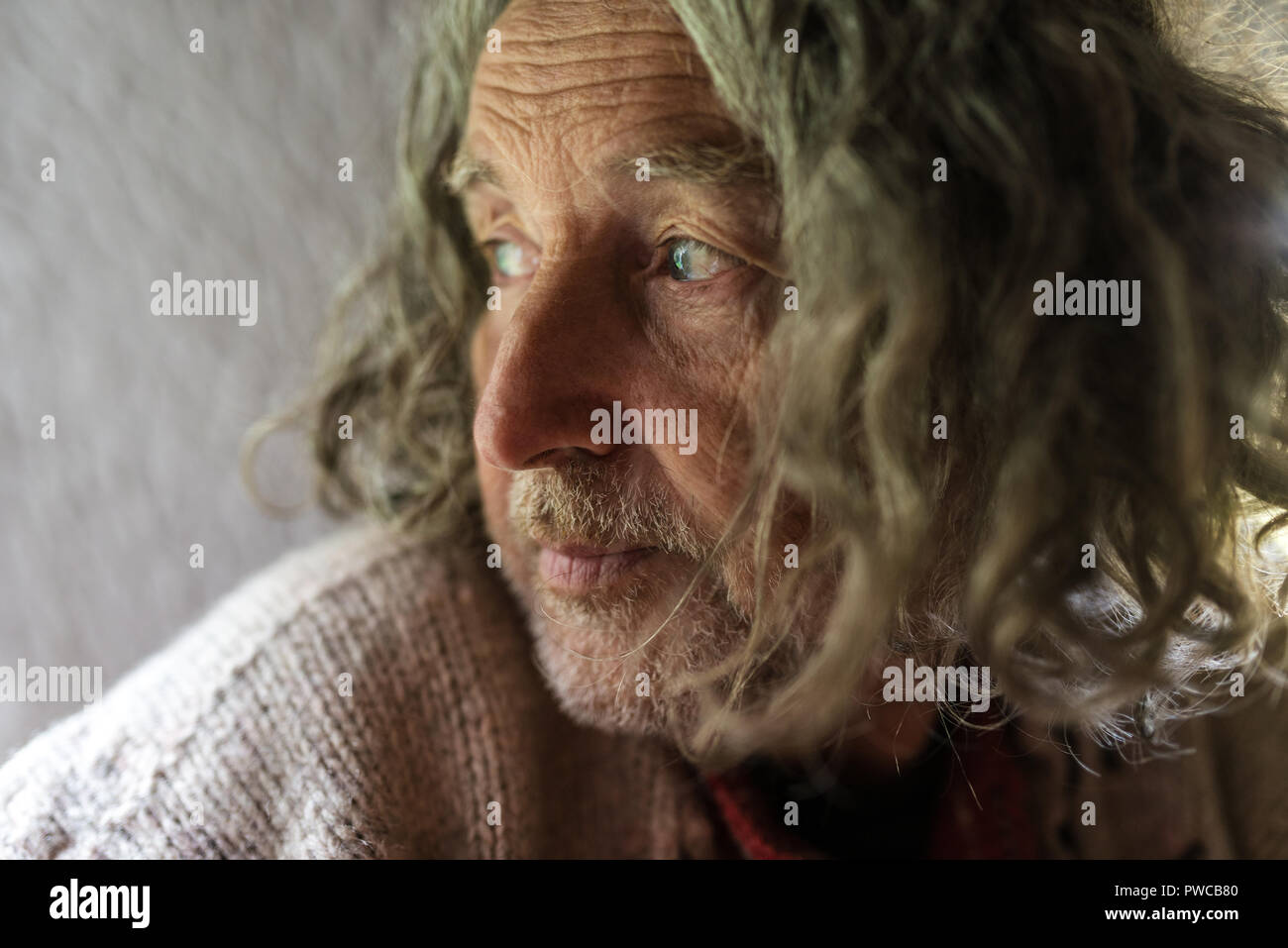 Portrait of old man wit long gray hair and stubble looking sad, side ...