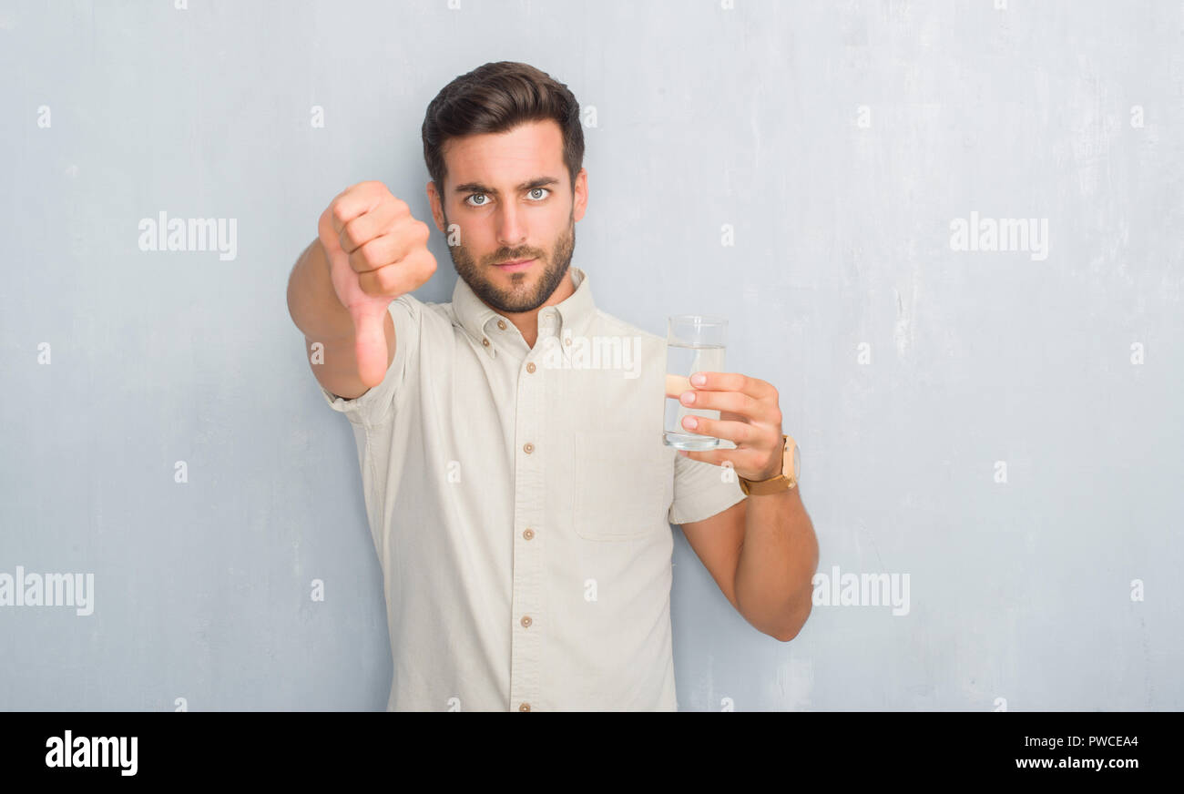 Handsome young man over grey grunge wall drinking glass of water with ...