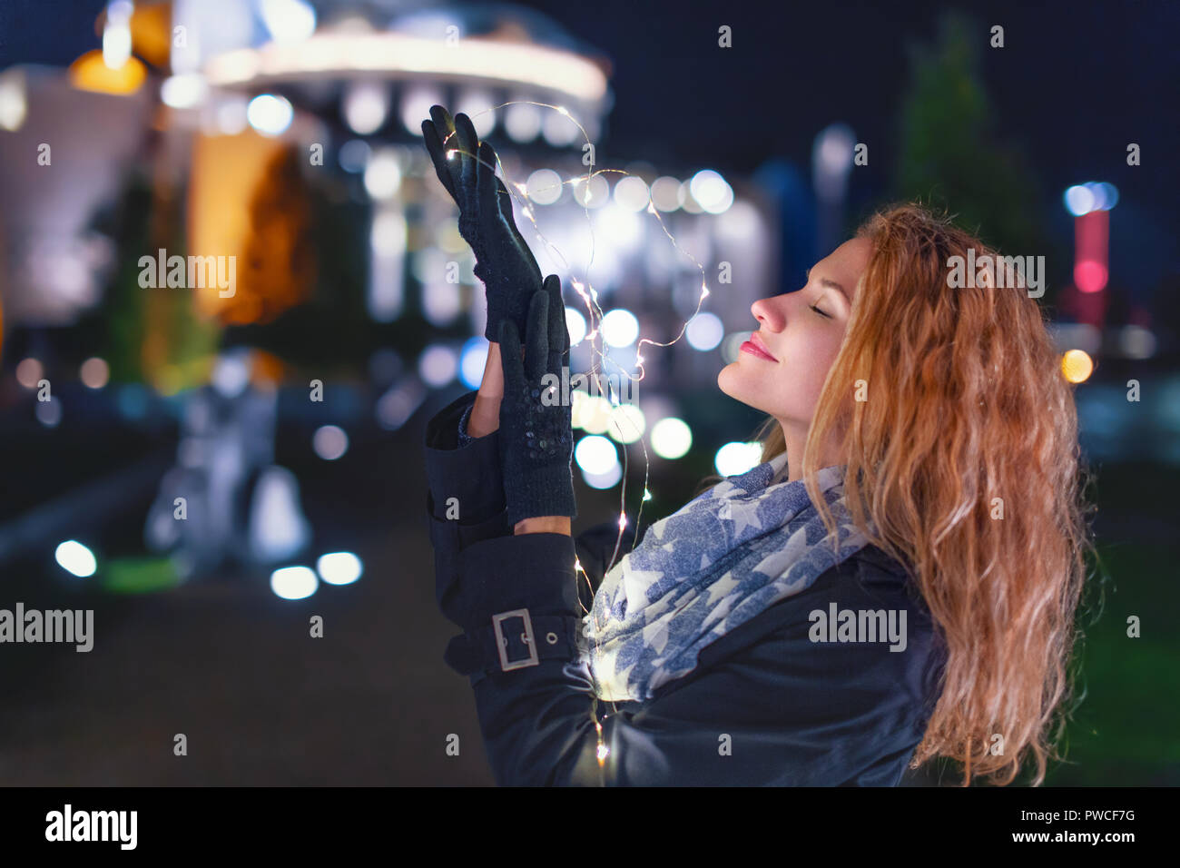 Young woman with fairy lights in cold city night imagine about ...