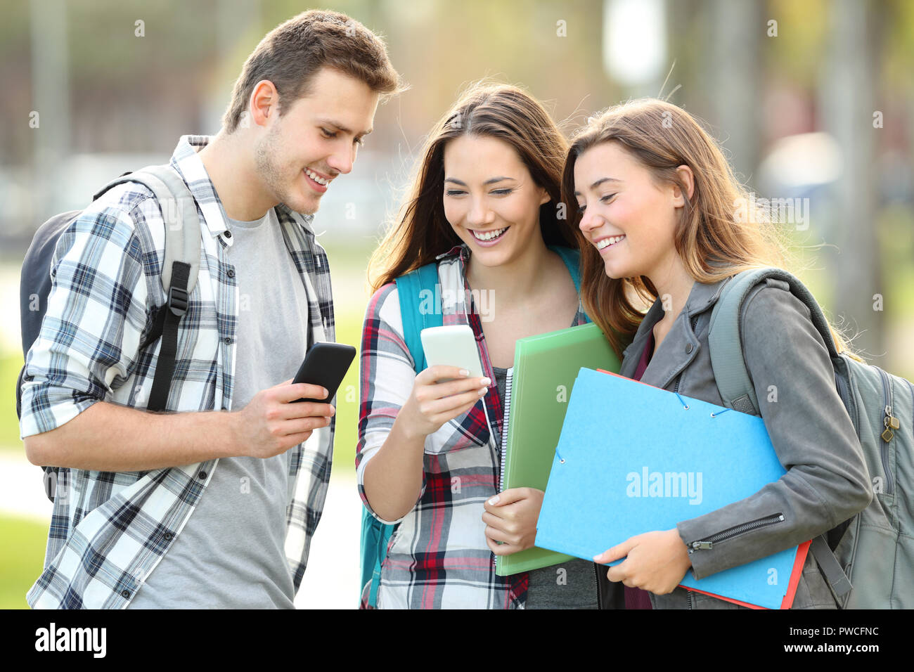 Three happy students watching media content in their smart phones in a ...