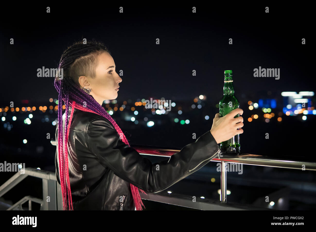 Portrait of lonely woman drinking alcohol from bottle at highway. A ...