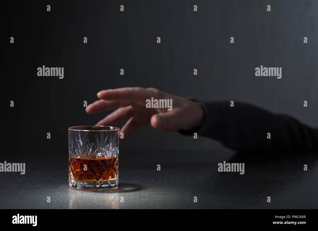 Man's hand reaches for a glass of alcohol. Conceptual image on the ...