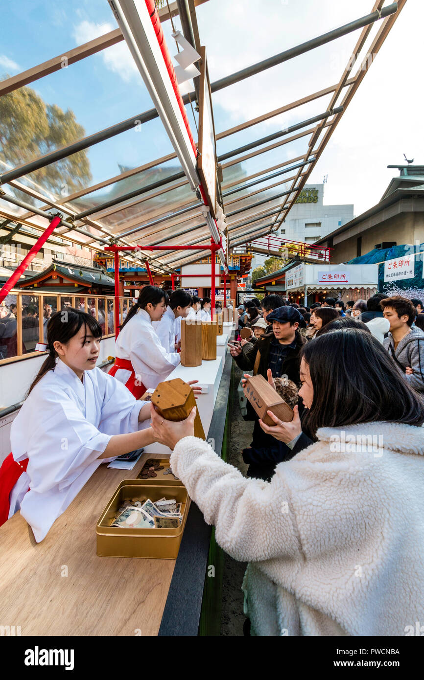 Japanese new year, shogatsu. Shrine Maidens, Miko, at busy counter selling Omikuji paper fortune ...
