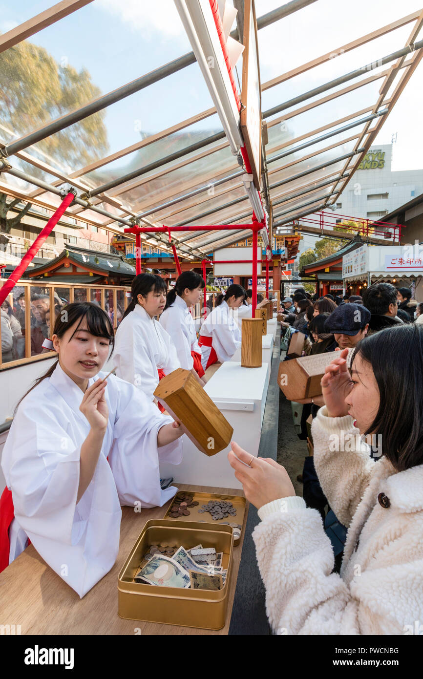 Japanese new year, shogatsu. Shrine Maidens, Miko, at busy counter selling Omikuji paper fortune ...